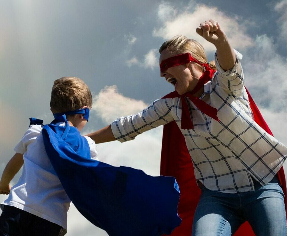Mother and son pretending to be superhero against cloudy sky with ...